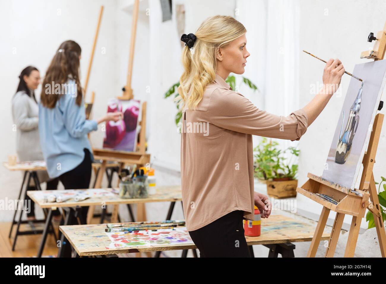 Side view of focused female artist painting on canvas on easel in art ...