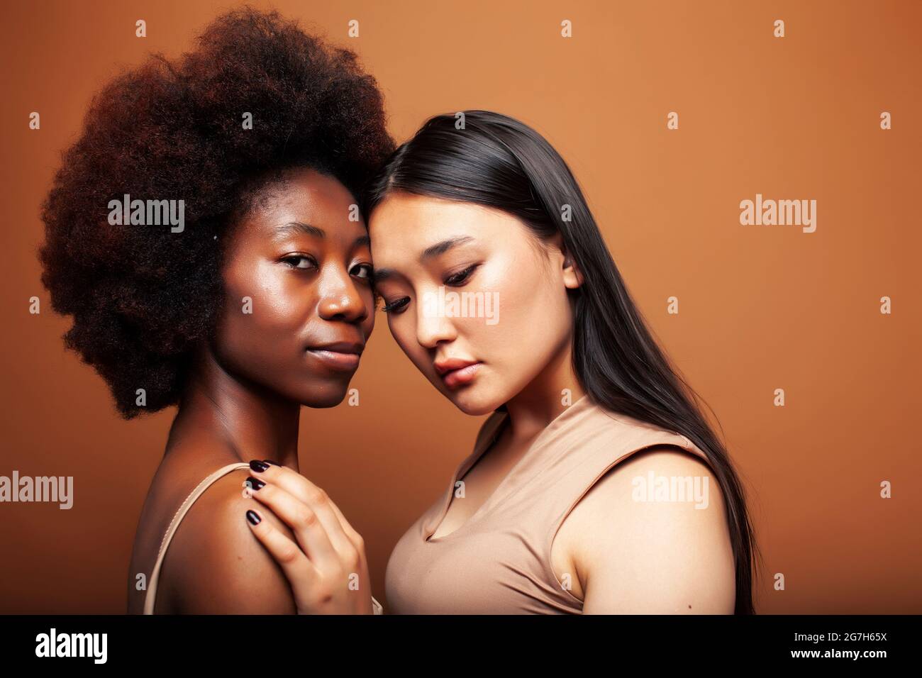 young pretty asian, afro woman posing cheerful together on brown ...