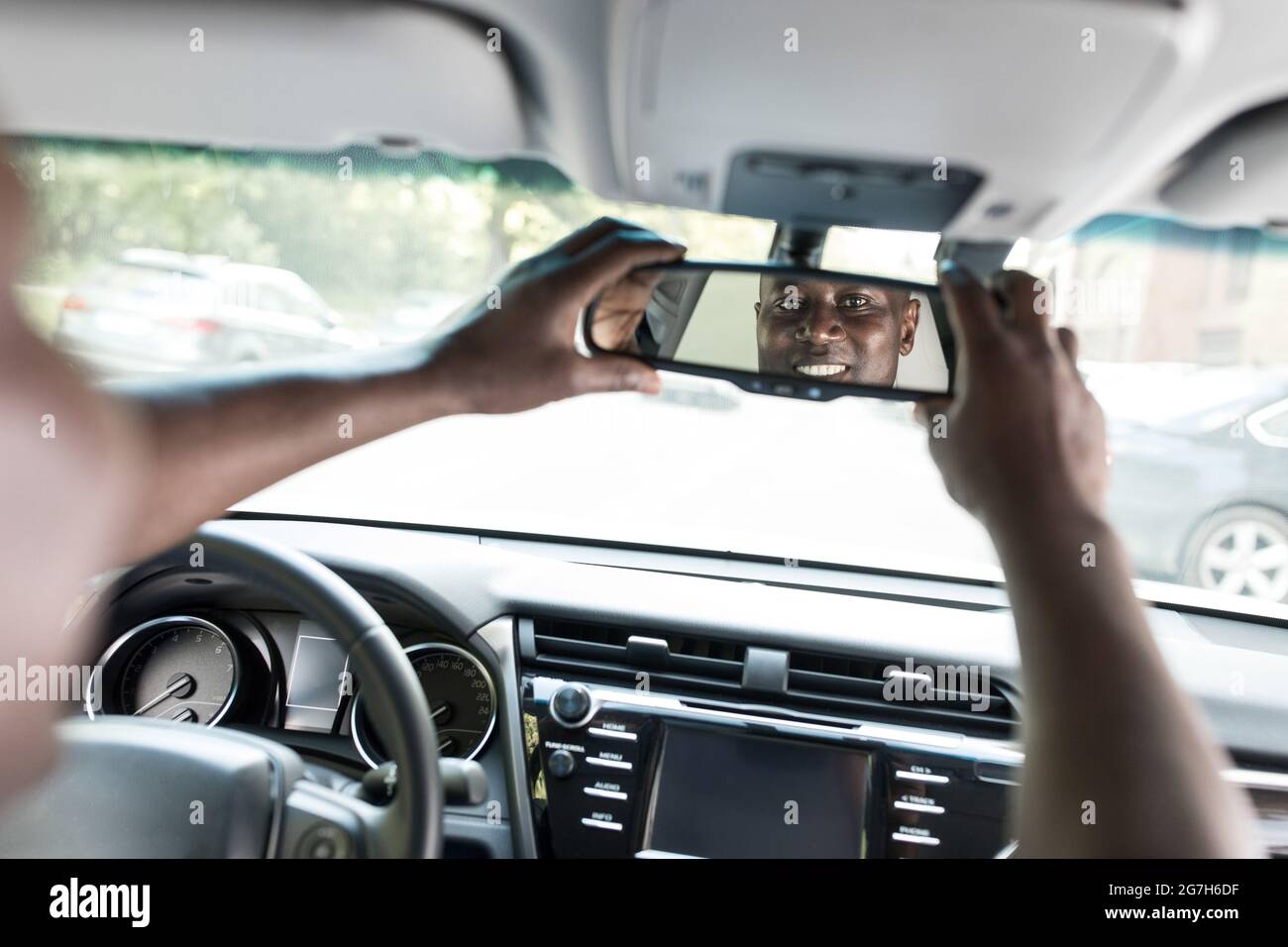 Smiling black guy adjusting rearview mirror in his car before driving ...