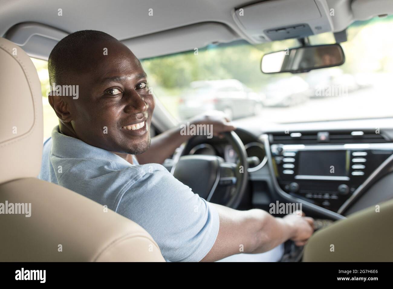 Cheerful black guy driver sitting inside brand new car, looking at back ...
