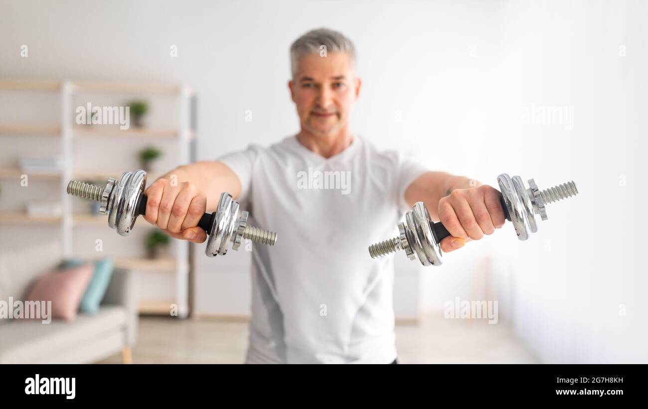 Sporty mature man lifting dumbells up over living room interior ...