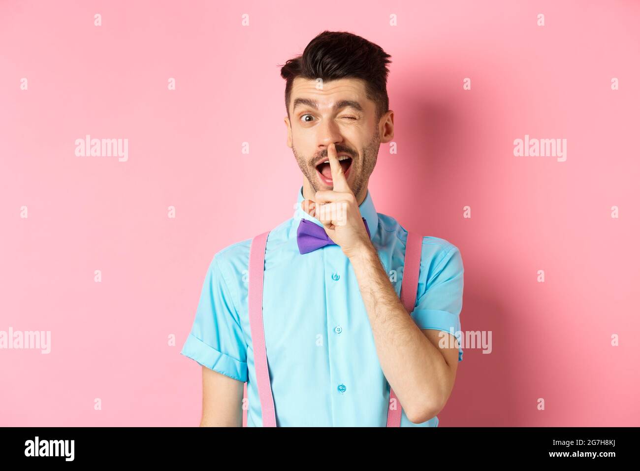Funny young man planning a surprise, hushing and winking at camera ...