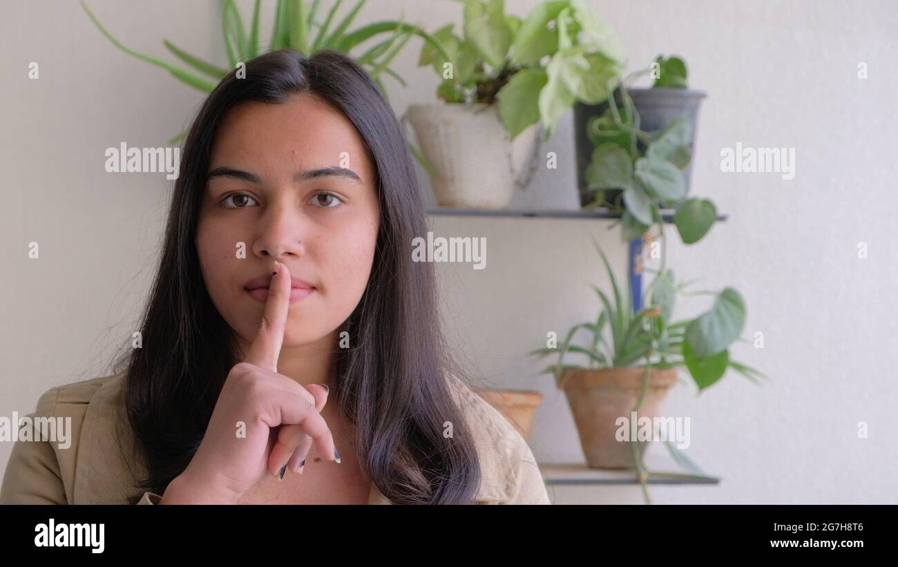 Pretty young Indian female with a hushing sign at home with house ...