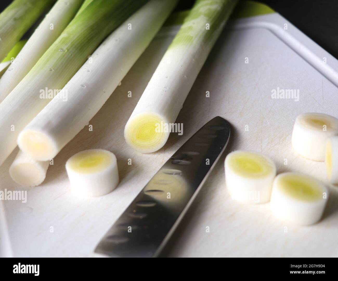 leeks on a chopping board with a sharp knife and some cut off parts ...