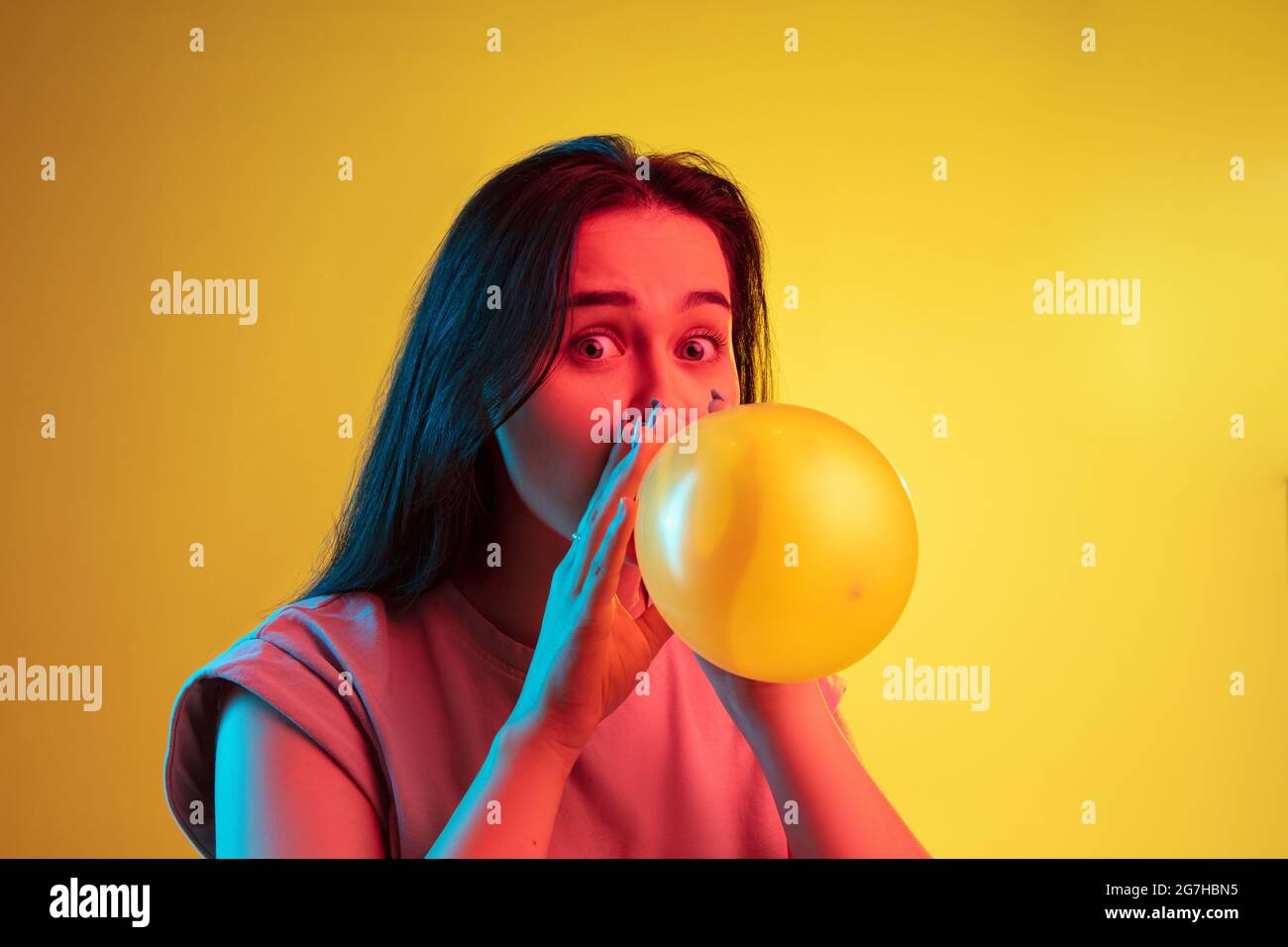 Inflating balloon. Young beautiful caucasian girl isolated on yellow ...