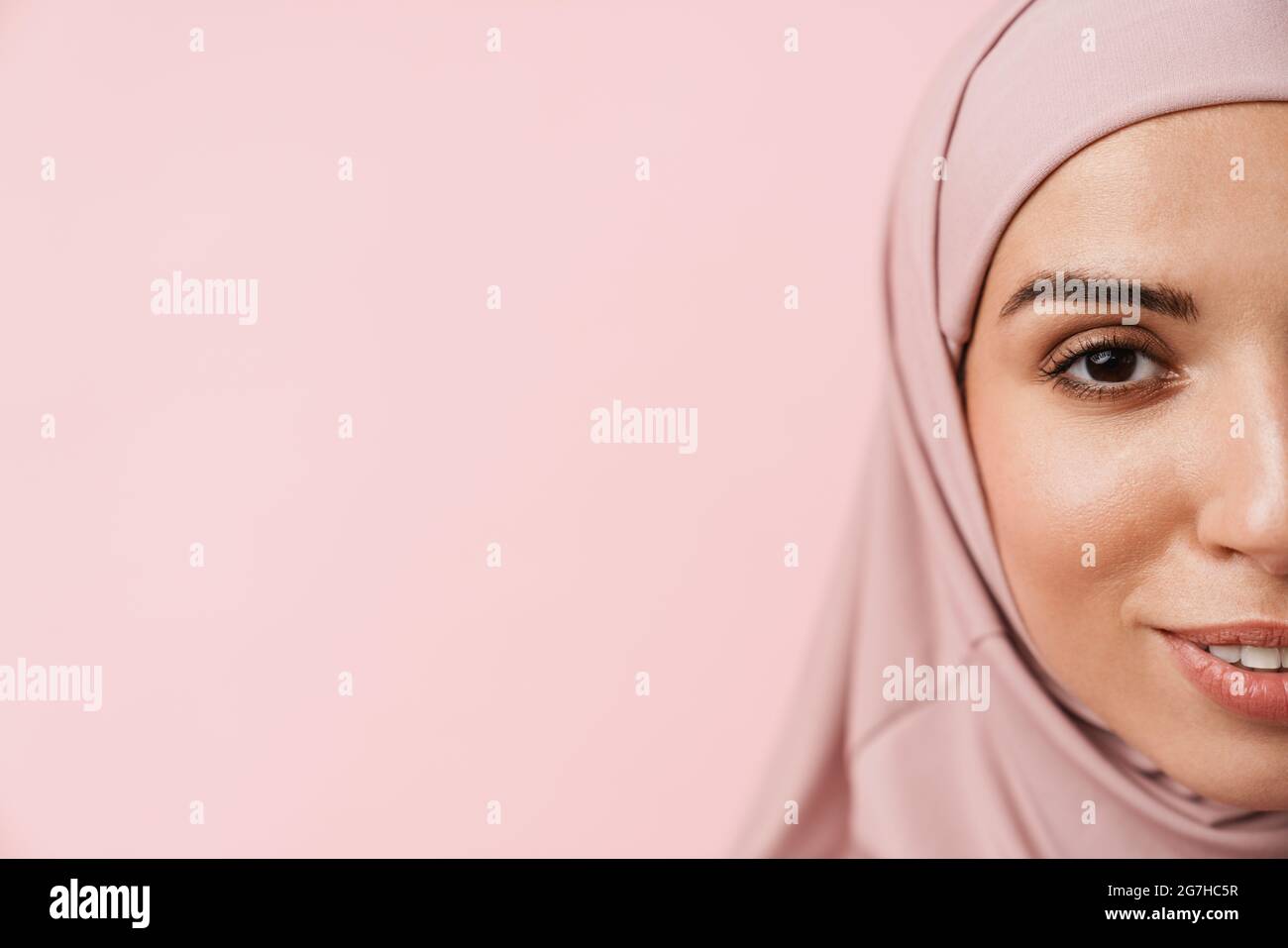 A half face portrait of smiling muslim woman in pink hijab looking at ...