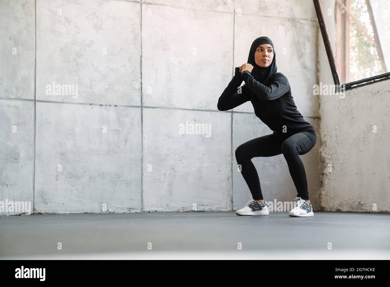 Young muslim woman in hijab doing exercise while working out indoors ...