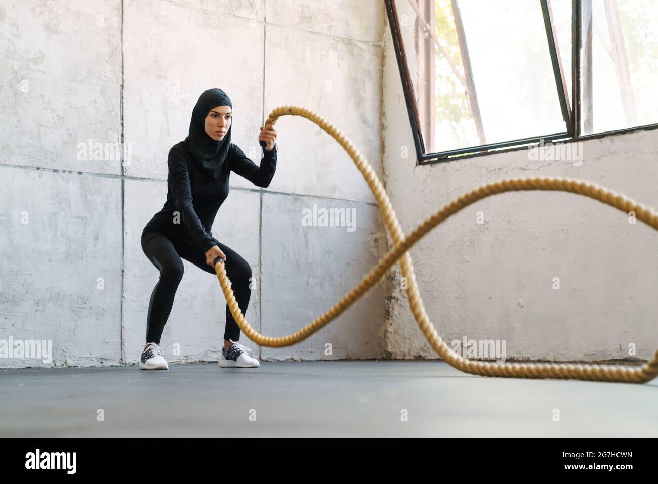 Young muslim woman in hijab working out with battle ropes indoors Stock ...