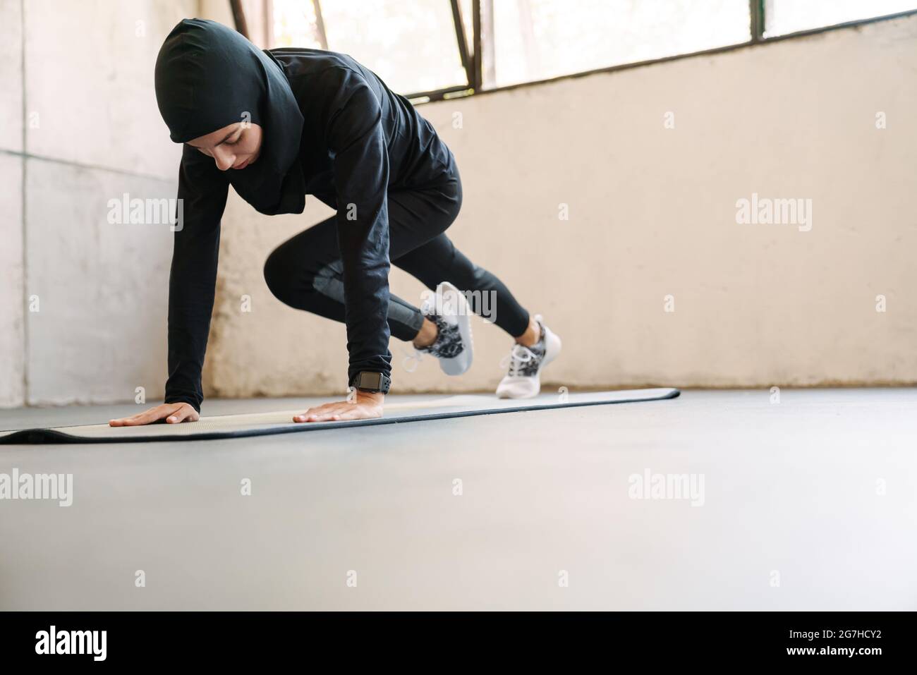Young muslim woman in hijab doing exercise while working out indoors ...
