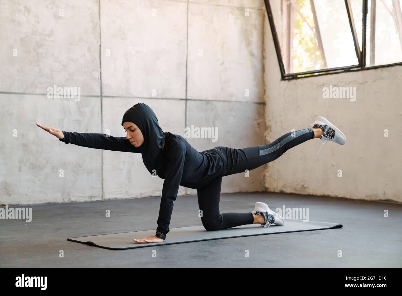 Young muslim woman in hijab doing exercise while working out indoors ...
