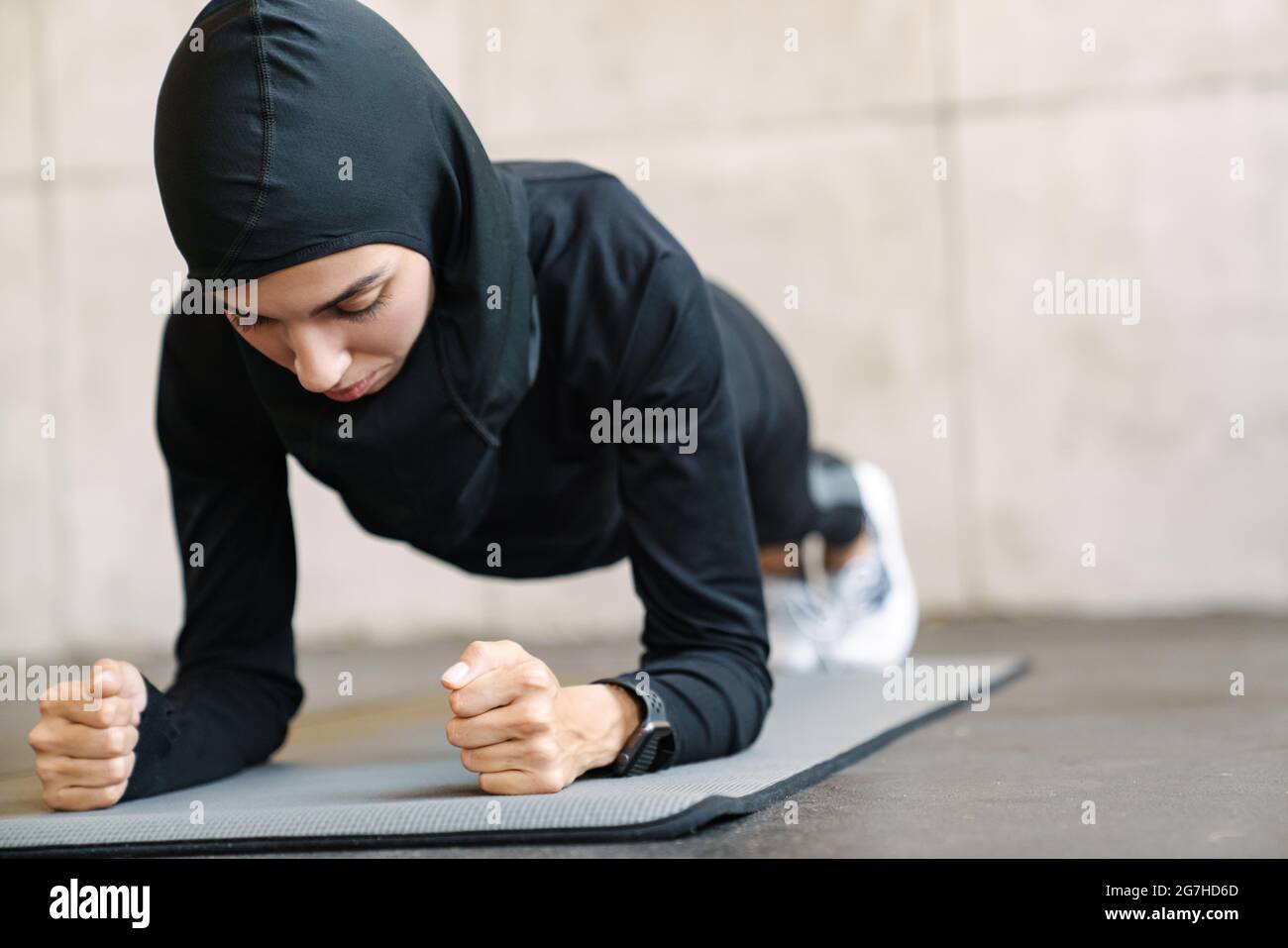 Young muslim woman in hijab doing exercise while working out indoors ...