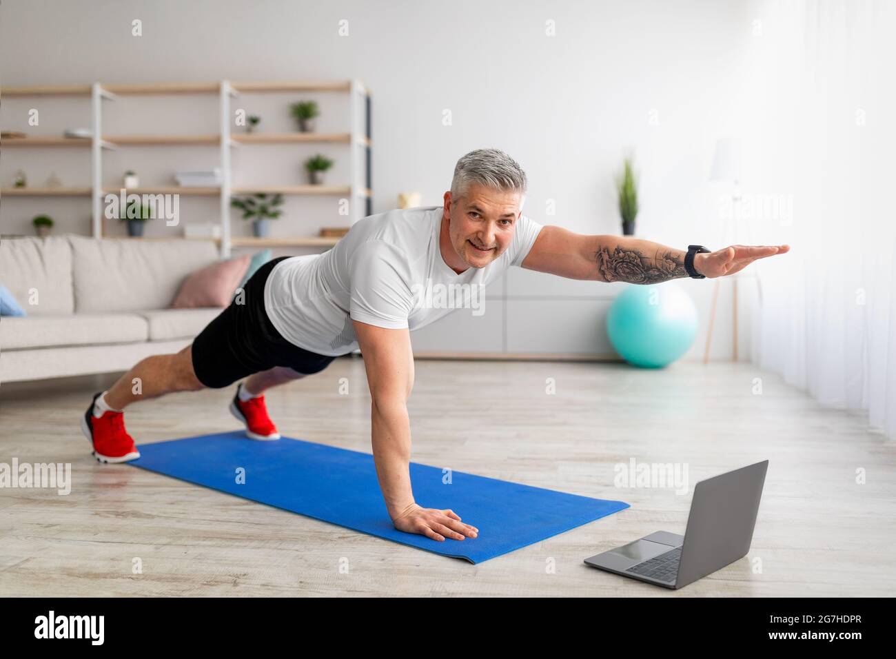 Domestic training. Happy mature man exercising to video on laptop ...