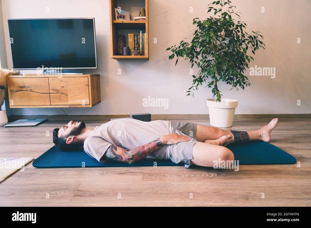 Bearded man meditating in Wind Relieving pose at home Stock Photo - Alamy