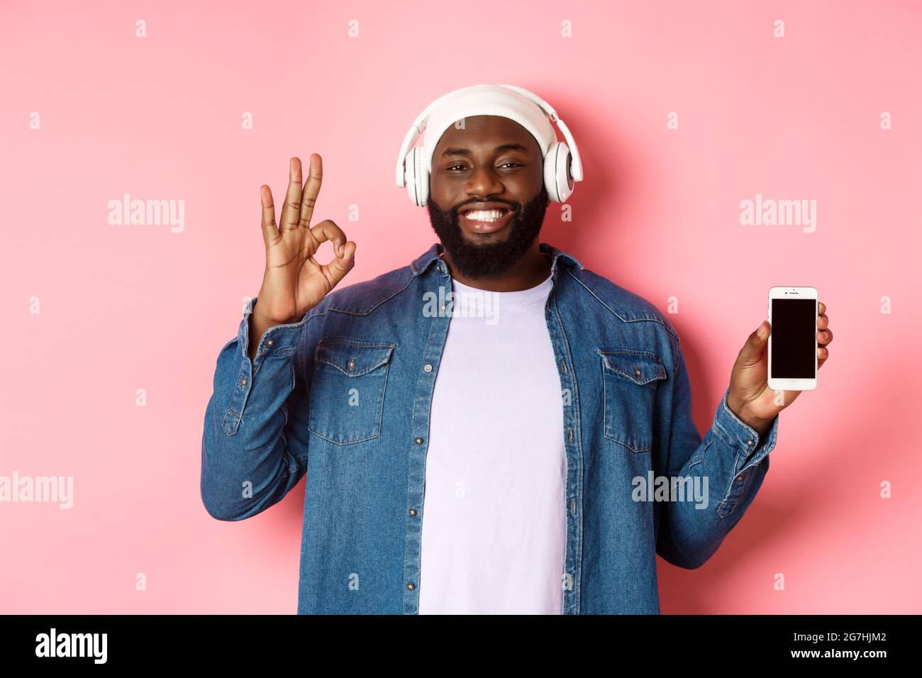 Happy hipster guy listening music on headphones and showing mobile ...