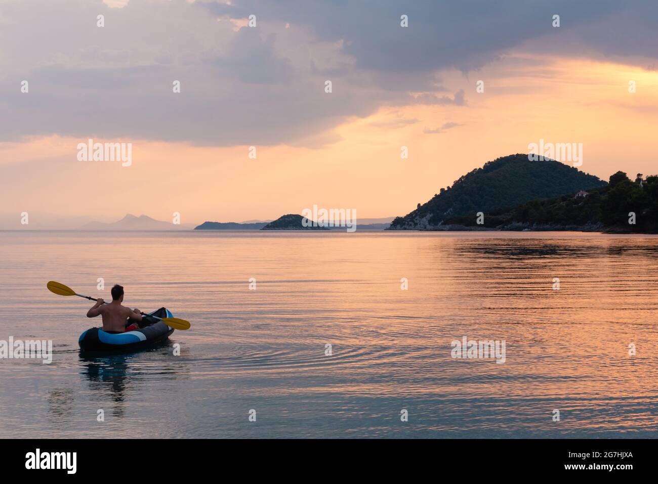 Young man riding a kayak in the calm sea and surrounded by islands at ...
