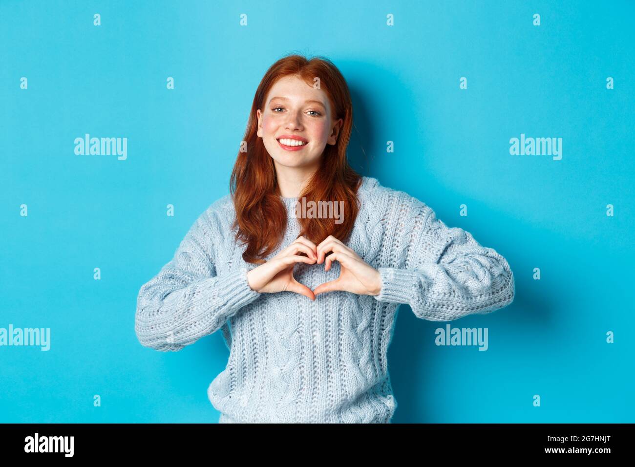 Cute redhead girl in sweater showing heart sign, I love you gesture ...