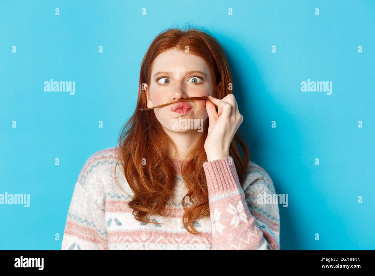 Close-up of silly and funny redhead girl making moustache with hair ...