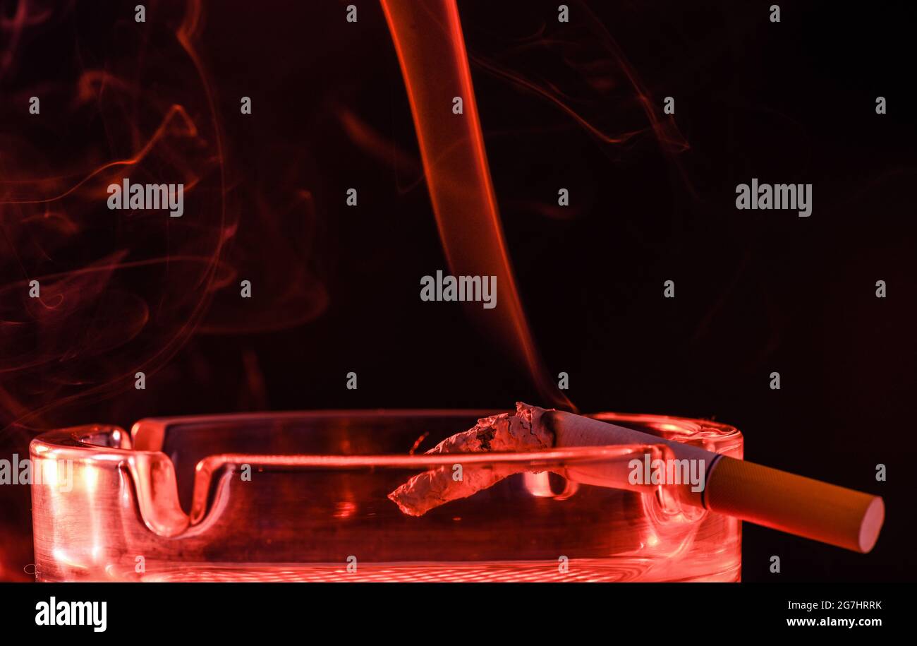 Red smoke rising from burning cigarette in glass ashtray maroon ...