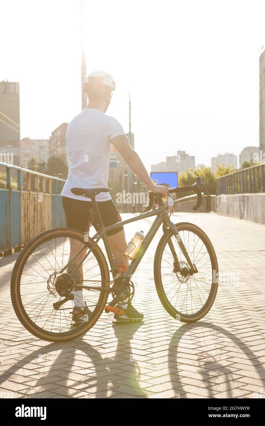Vertical rear view shot of a male cyclist in helmet standing with his ...