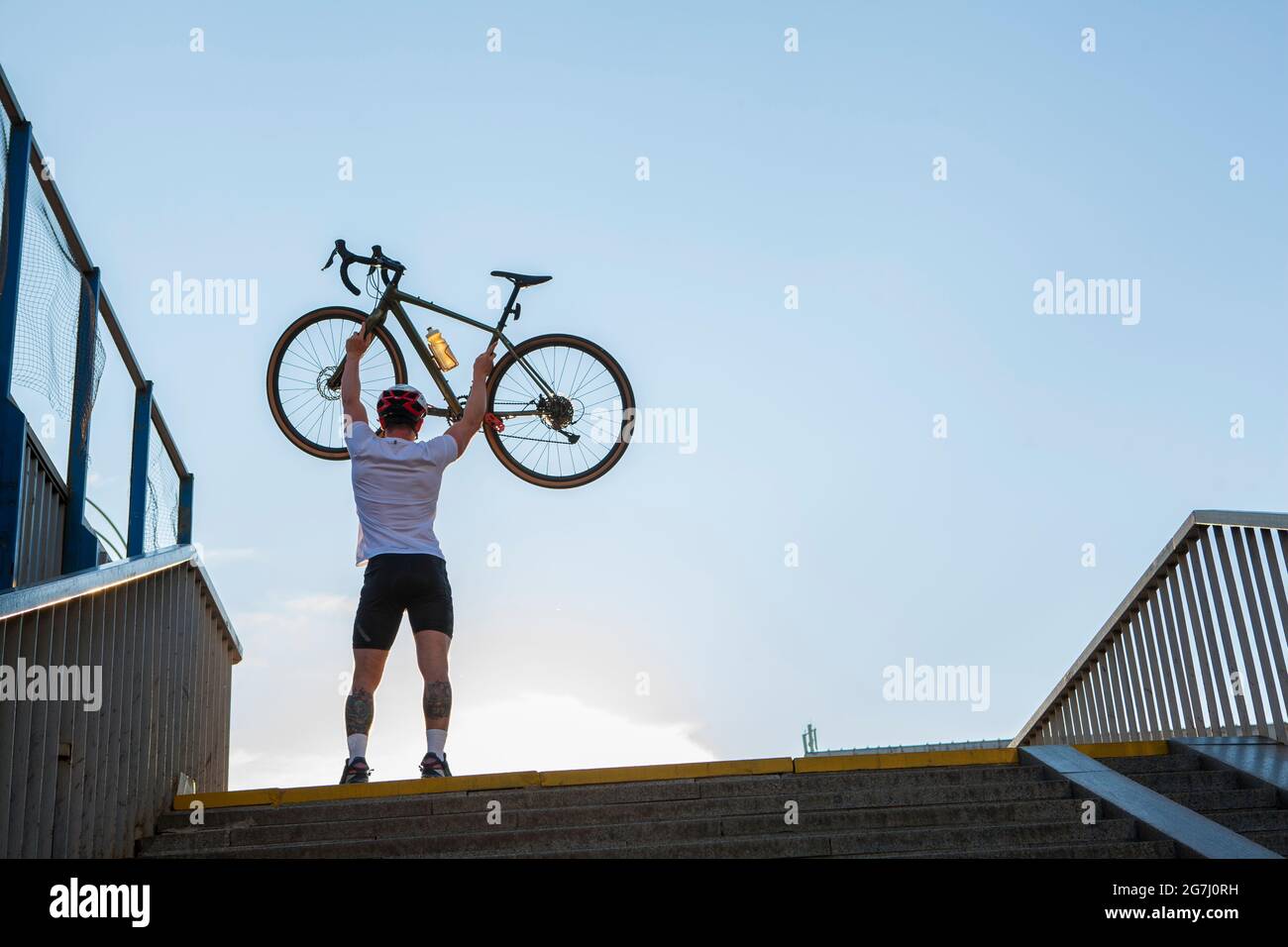 Rear view full length shot of an athletic man lifting his bicycle in ...