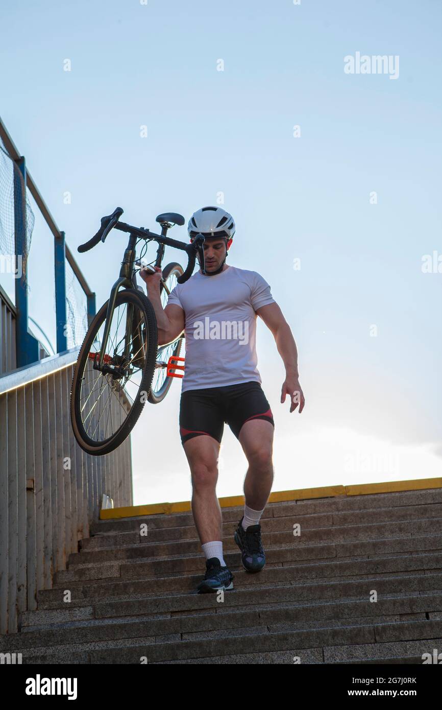 Vertical low angle shot of a muscular cyclist carrying his bike down ...