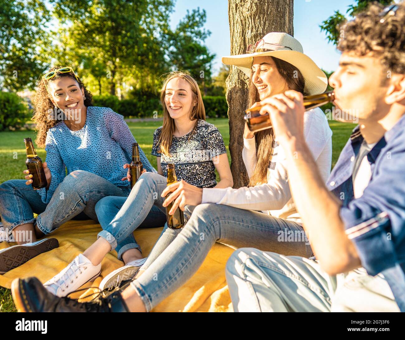 Happy friend group outdoor in city park drinking beer from bottle ...