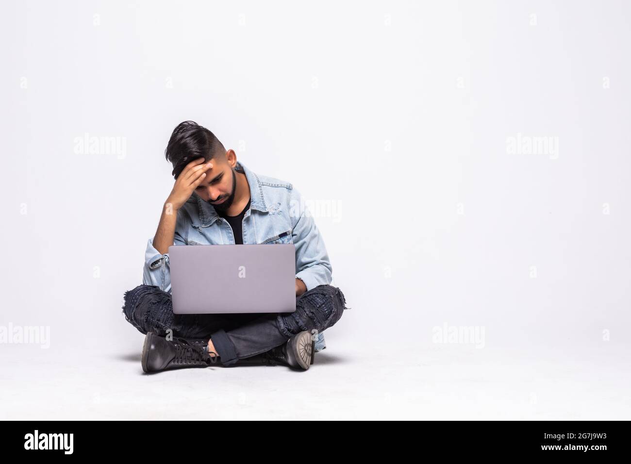 A young man sitting on the floor with a crossed legs putting his laptop ...