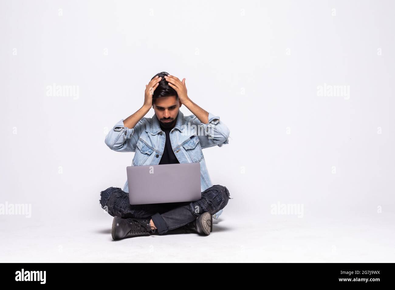 A young man sitting on the floor with a crossed legs putting his laptop ...
