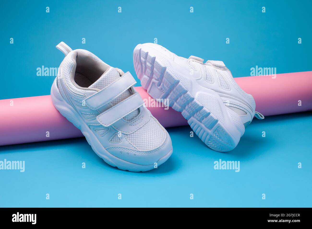 side view of two white unisex running shoes on a pink long paper tube ...