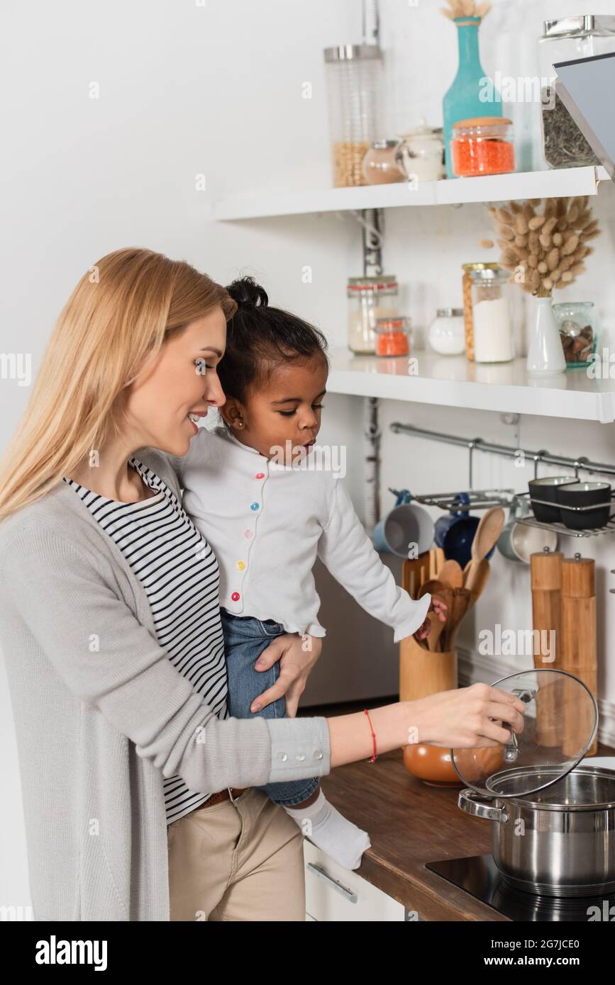 happy woman holding adopted and surprised african american kid while ...