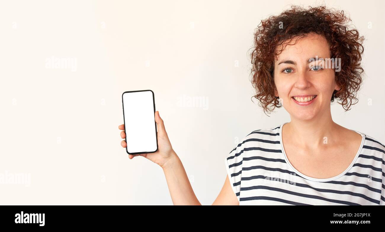 A woman poses next to her mobile phone, looking at the camera Stock ...