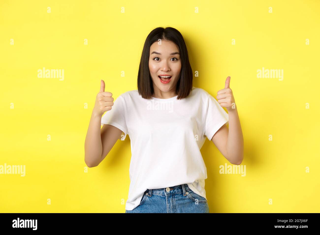 Pretty young asian woman in white t-shirt, showing thumbs up and ...