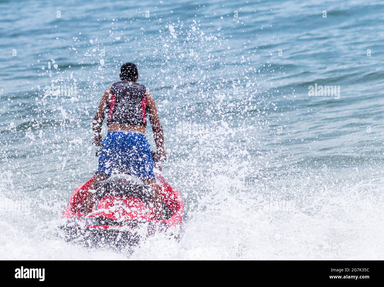 Backshot of a man jet skiing with blue swimming trunks on a red ...