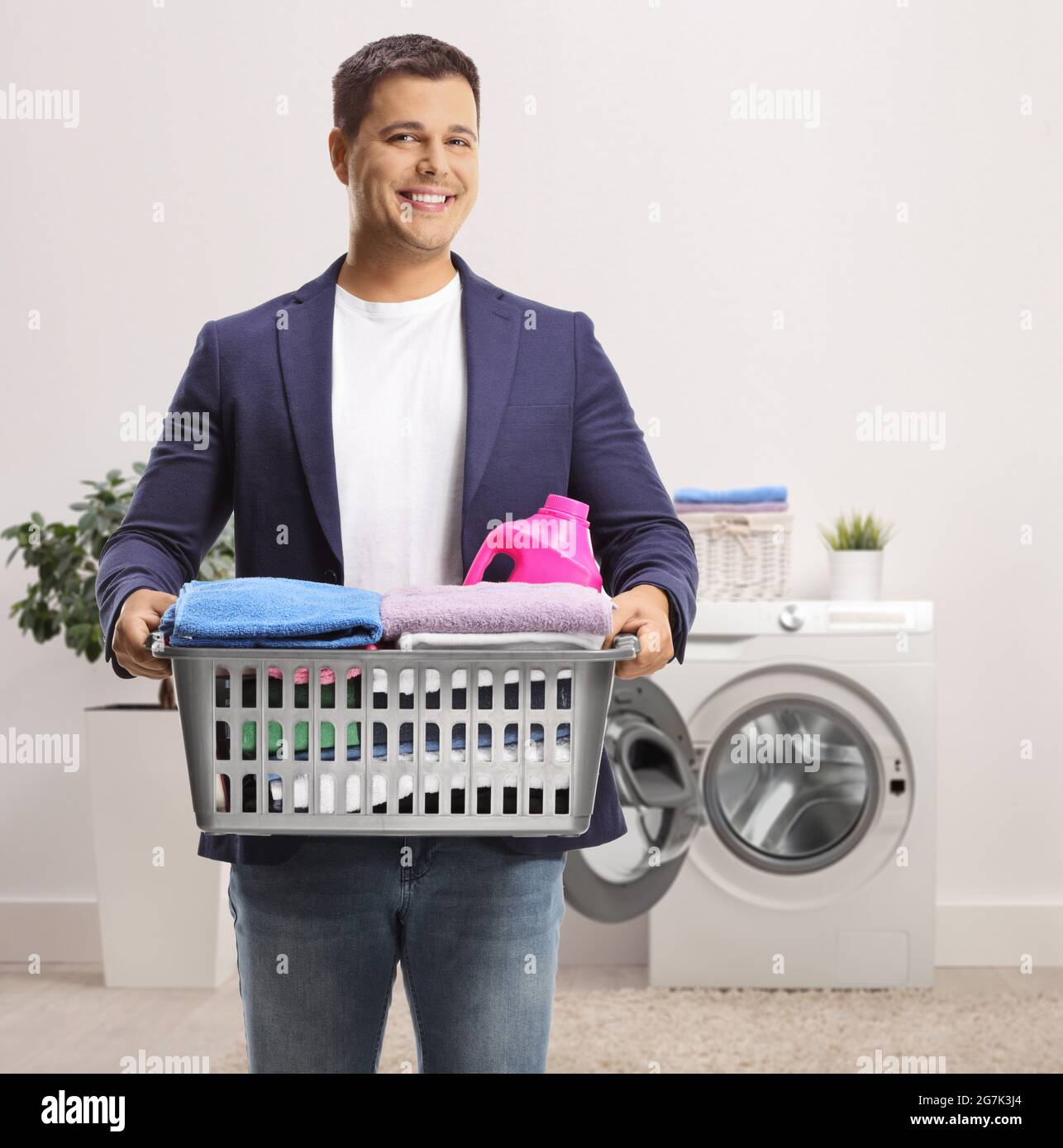Young man carrying a laundry basket with clothes and standing in a ...