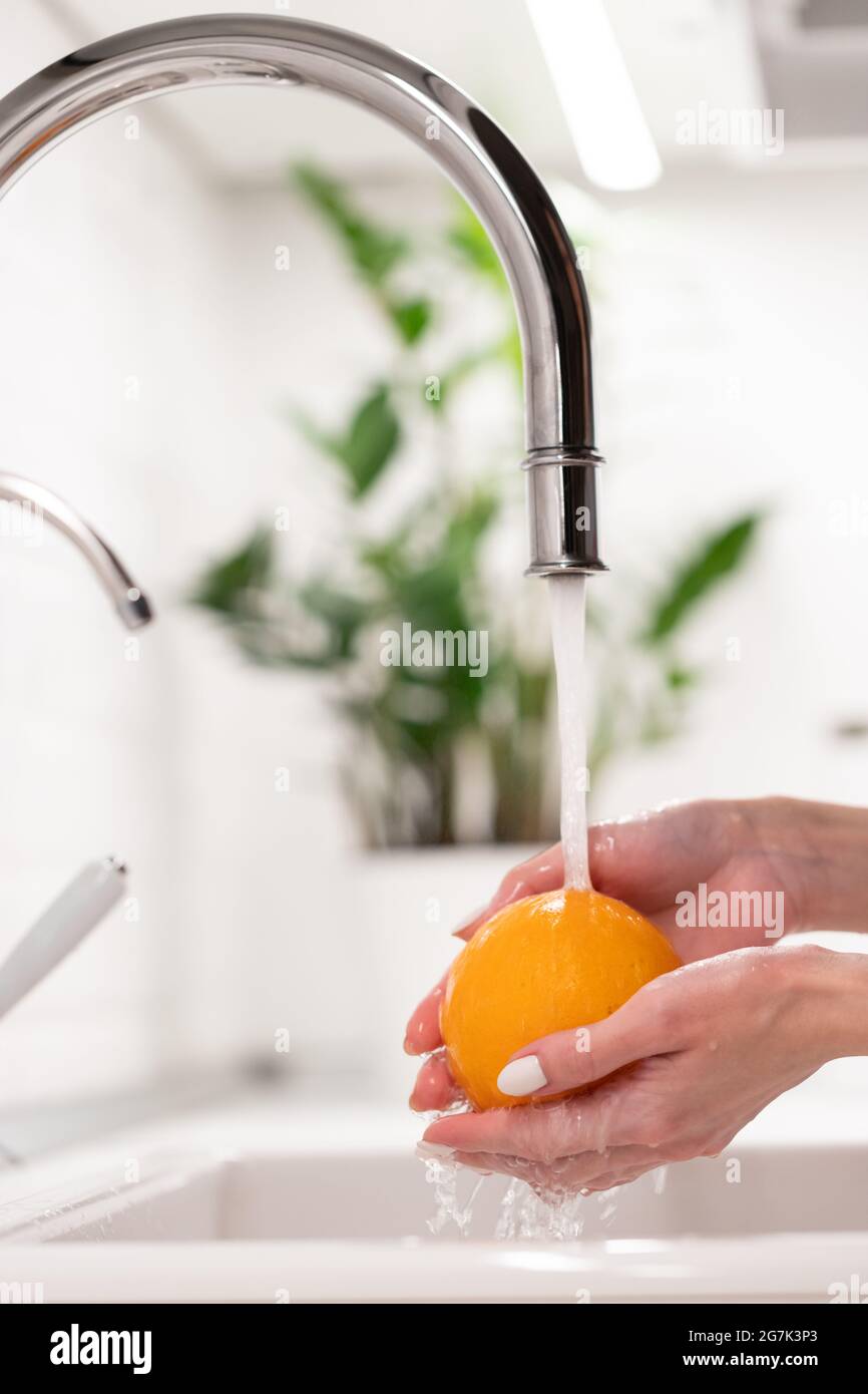 Female washing orange fruit in fresh water from kitchen sink crane ...