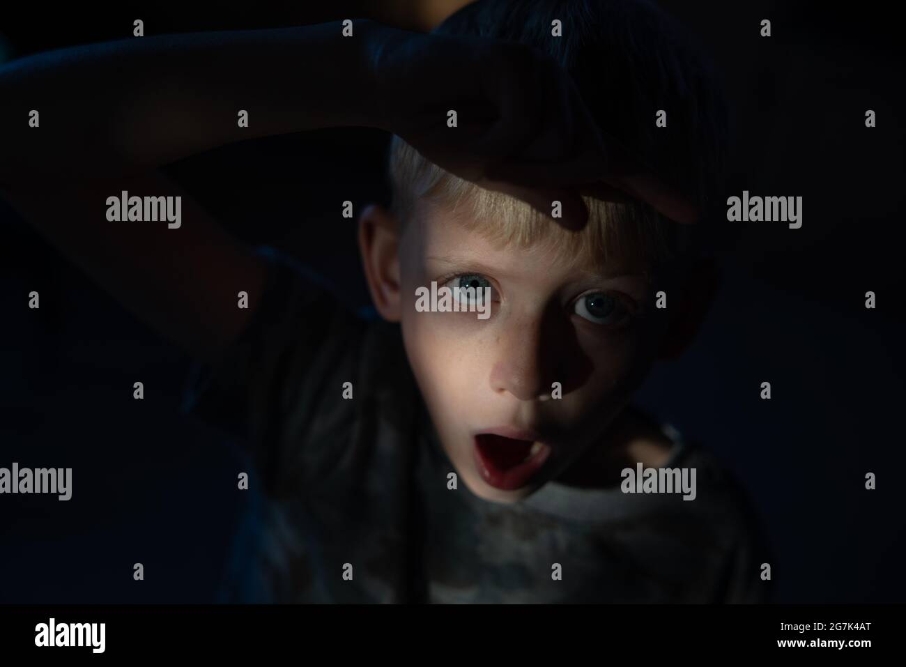 Scared blue-eyed child looking up against a dark background - concept ...