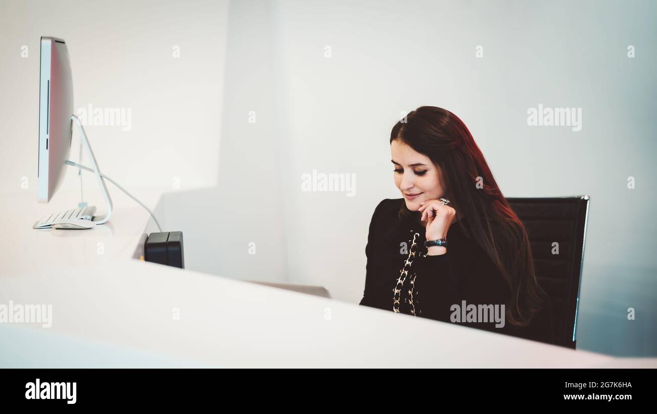 A charming female receptionist with long hair is working on her netbook ...