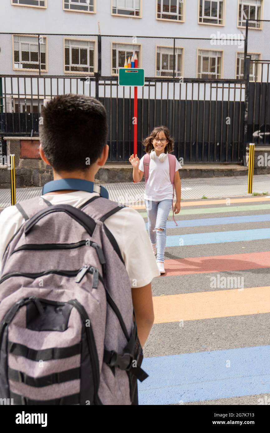 Two Caucasian children, classmates, greet each other in a crosswalk in ...