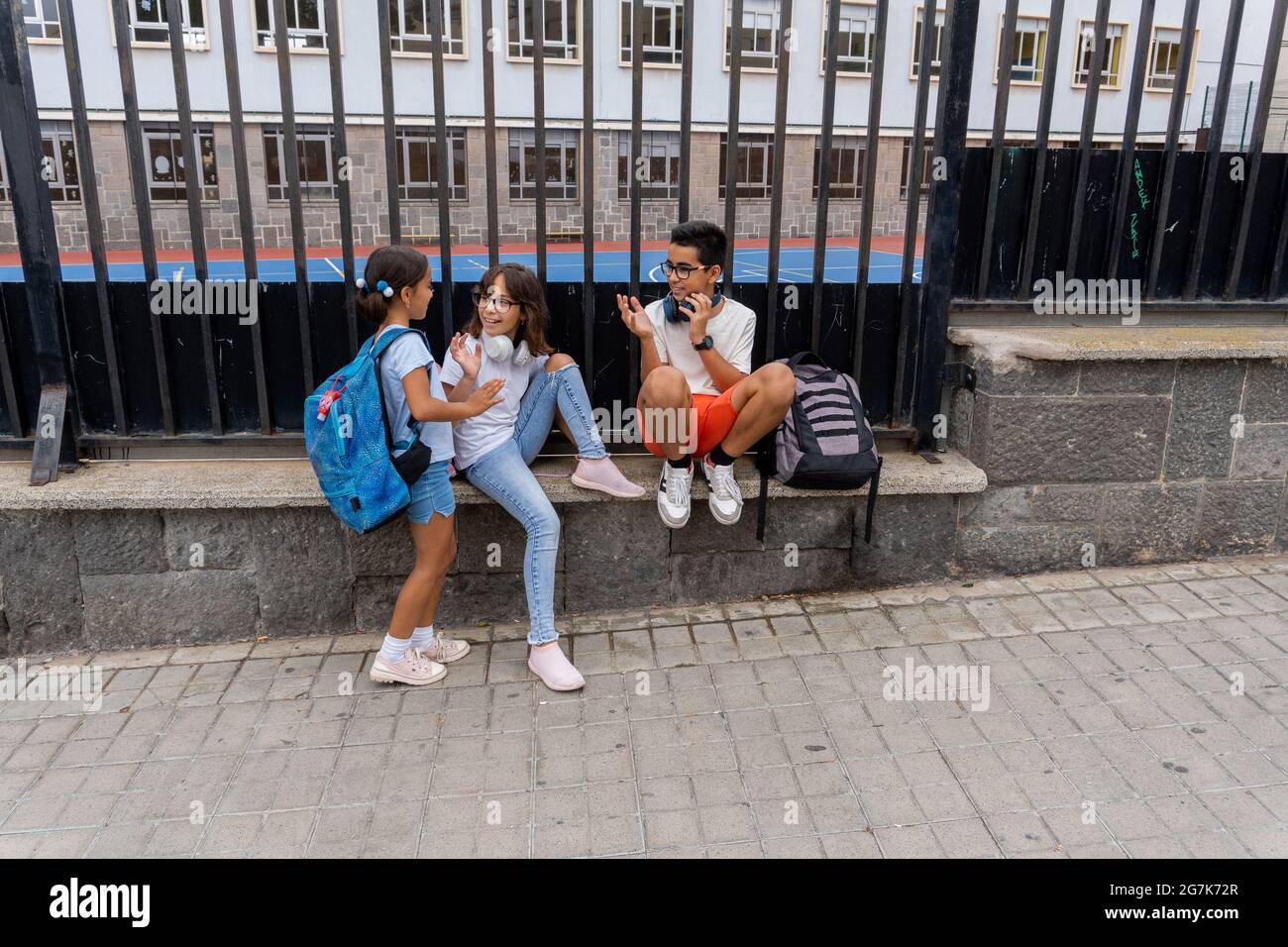 Three Caucasian children greeting and talking at the school gate. Back ...