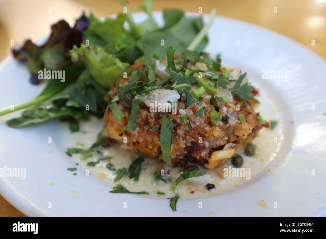 Closeup shot of plated crab cake with a garnish of greens at an upscale ...