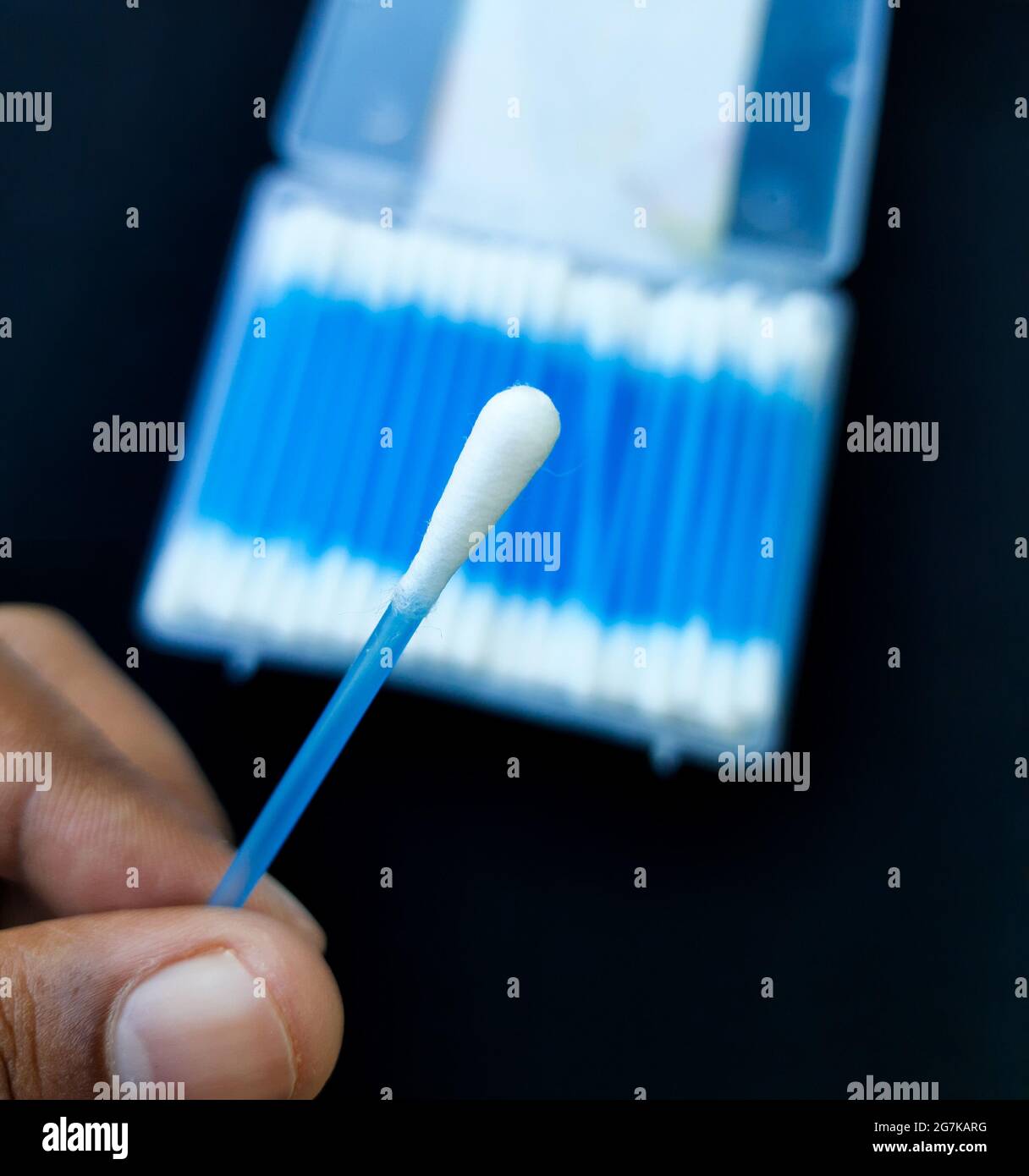 Shallow focus of male fingers holding a cotton swab tool with blurred ...