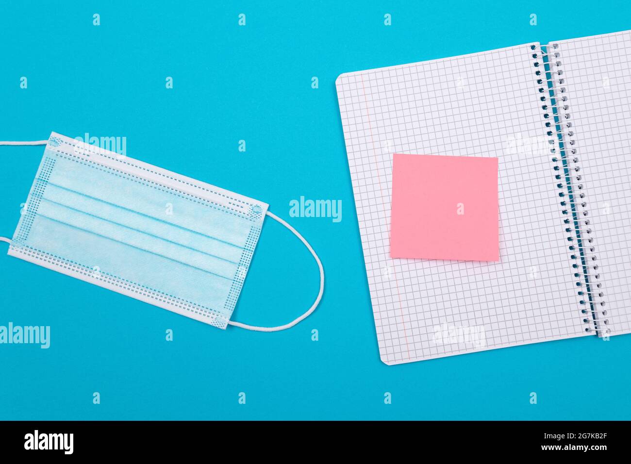 A Medical Mask and a Note Pad with Sticky Note Lying on Blue Table ...