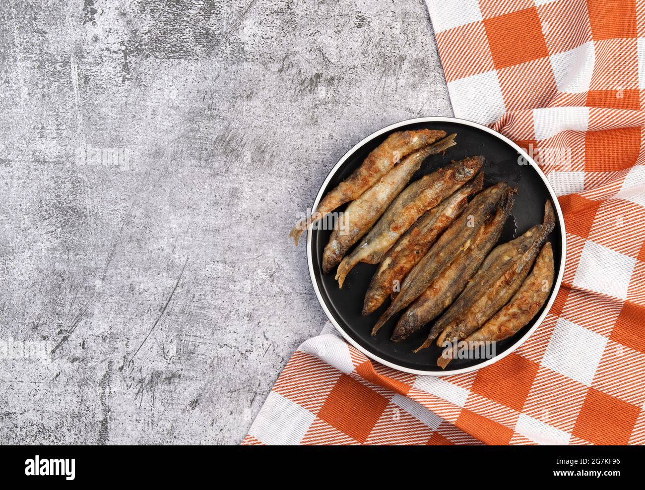 Pan fried capelin or smelt fish on a round plate on a dark grey ...