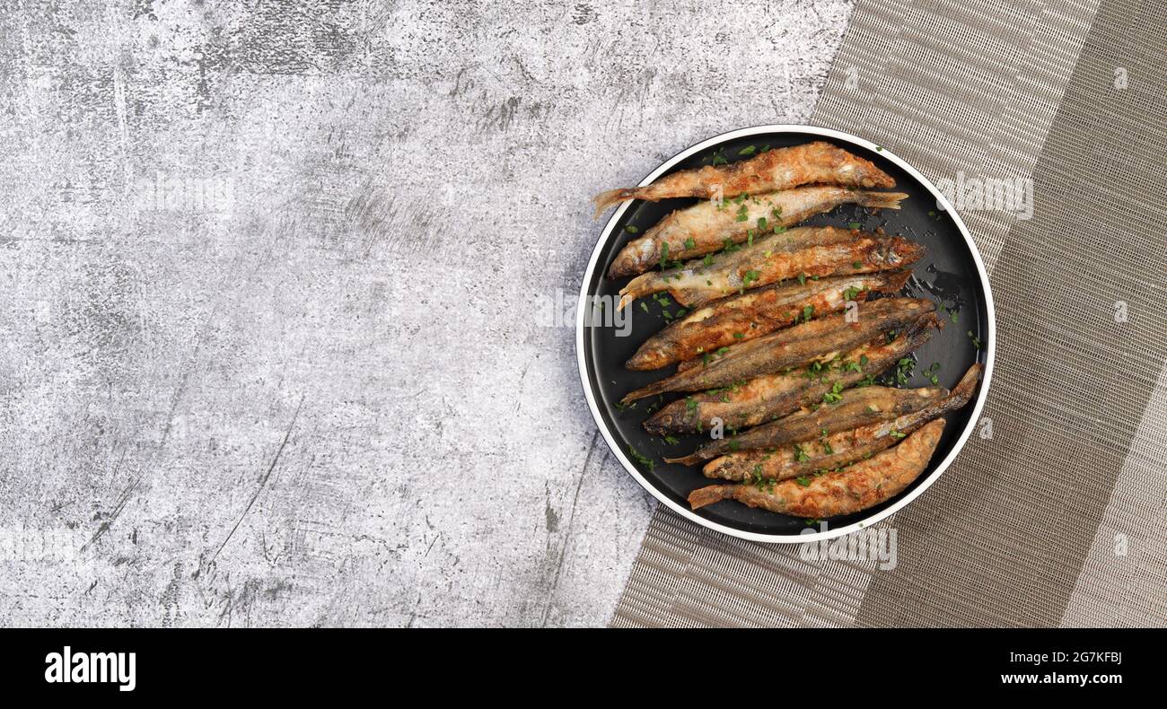 Pan fried capelin or smelt fish on a round plate on a dark grey ...