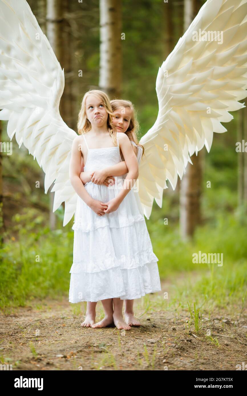 Vertical shot of two Caucasian blonde girls in angel wings costume in a ...