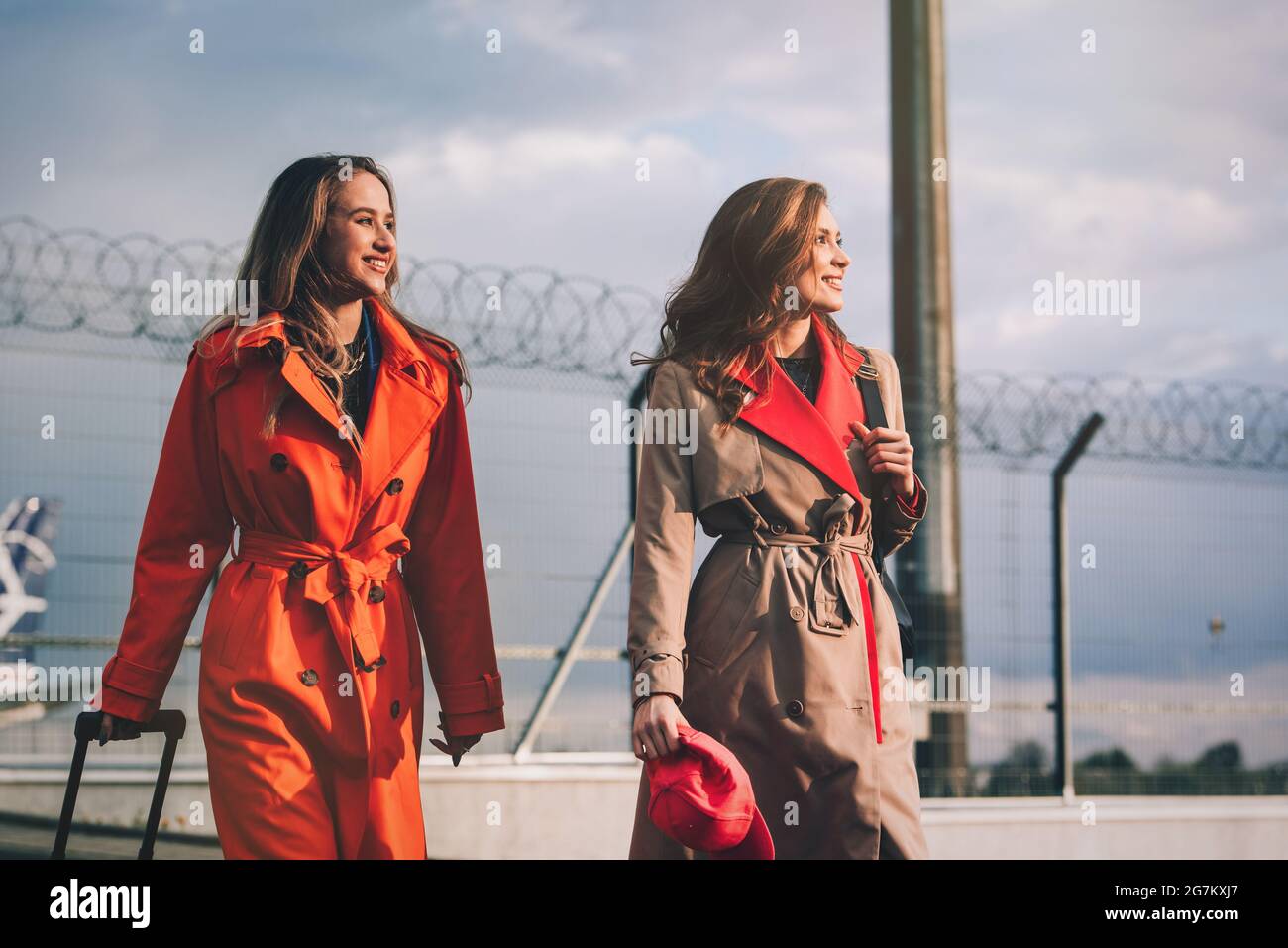 Two happy girls walking near airport, with luggage. Air travel, summer ...