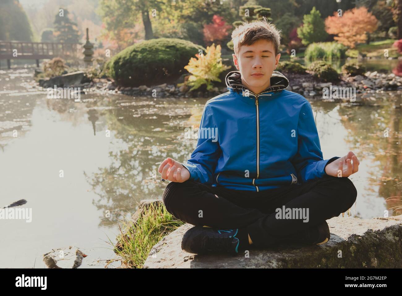 Teenage boy meditating and relaxing in a city park japanese garden ...