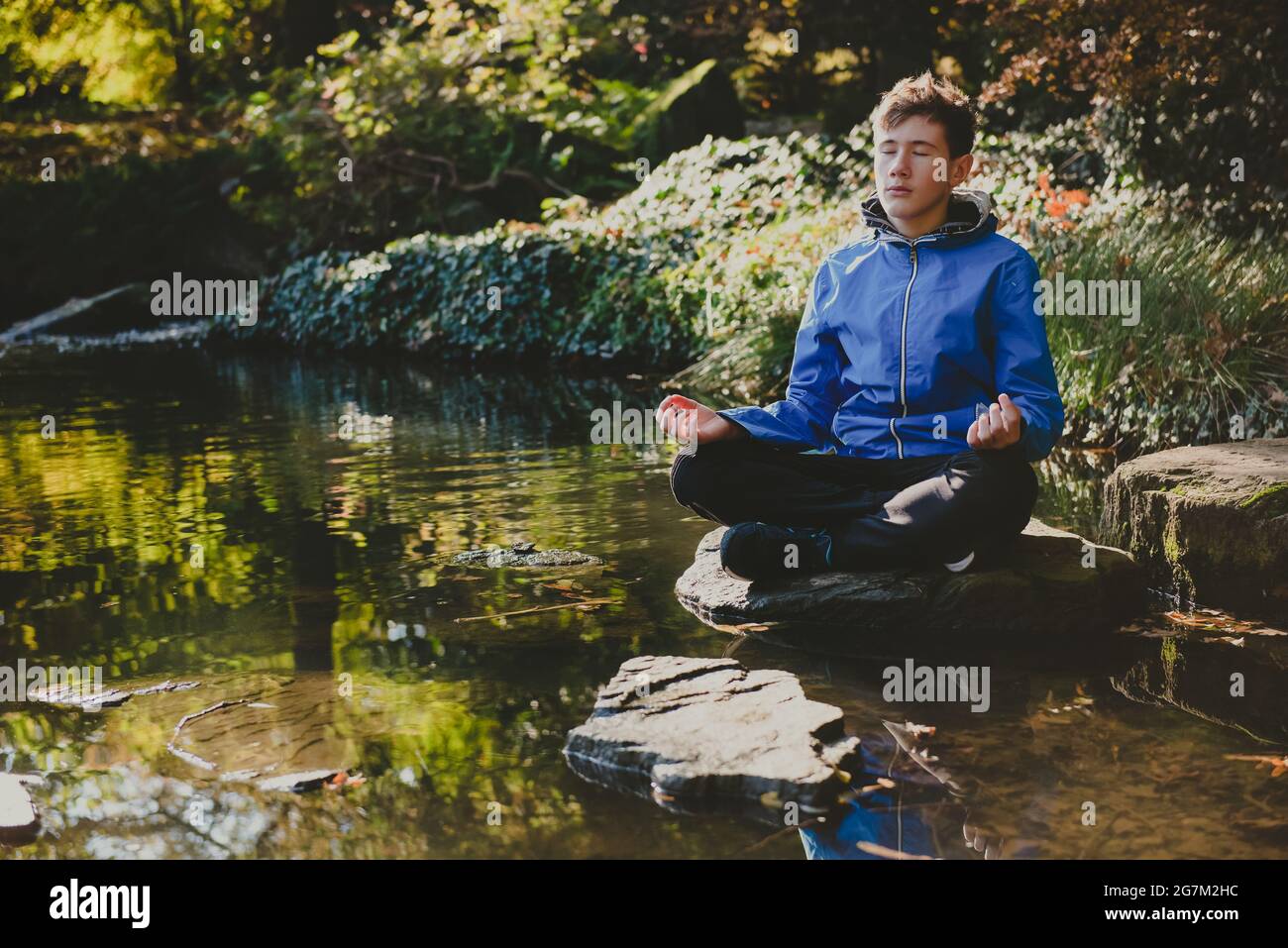 Teenage boy meditating and relaxing in a city park japanese garden ...