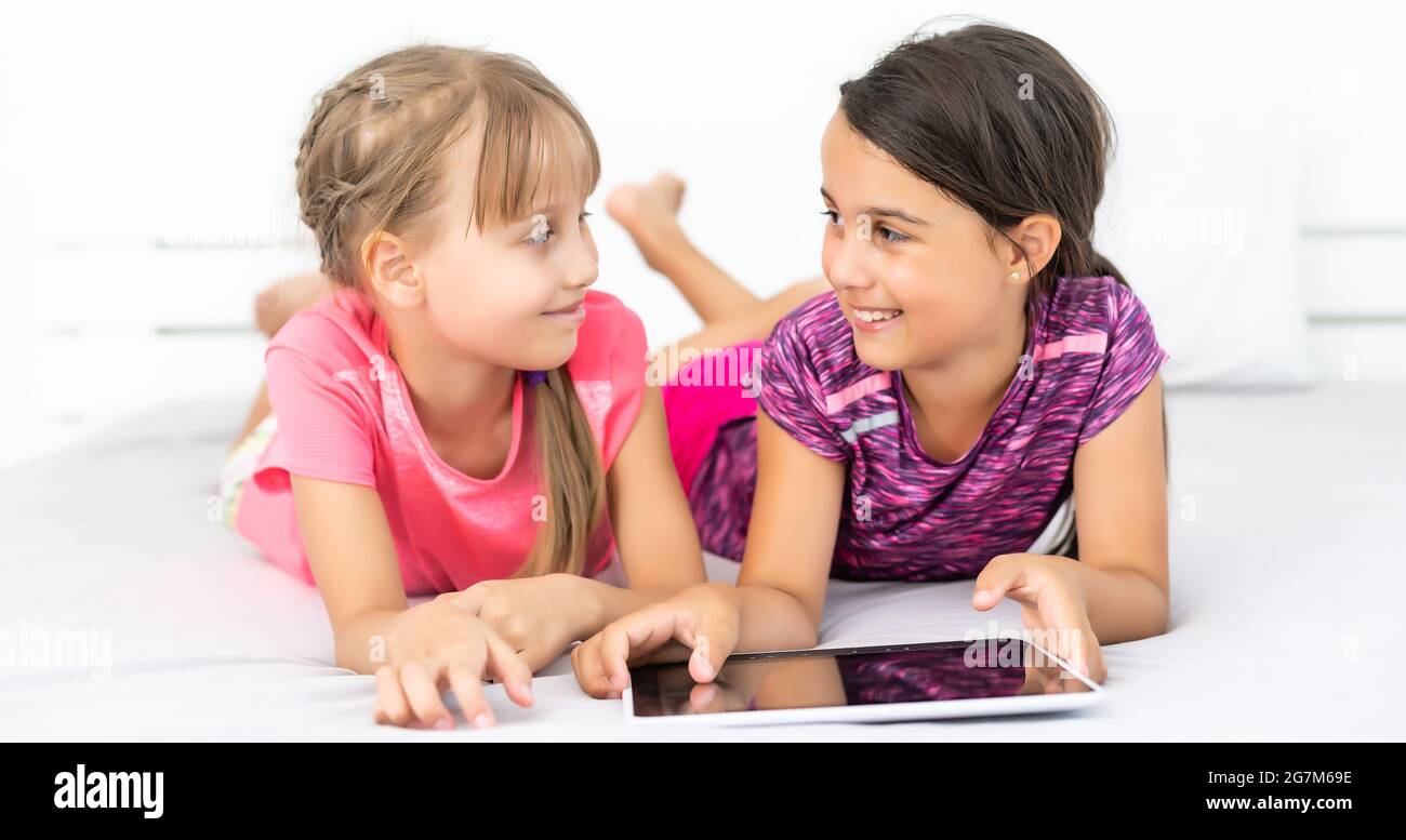 Two cute little girls are using a digital tablet and smiling while ...