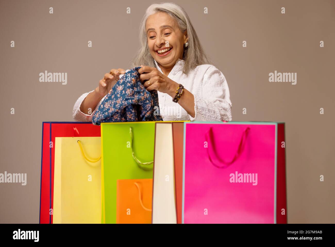 An old woman behind colorful handbags endearingly holding her new cloth ...
